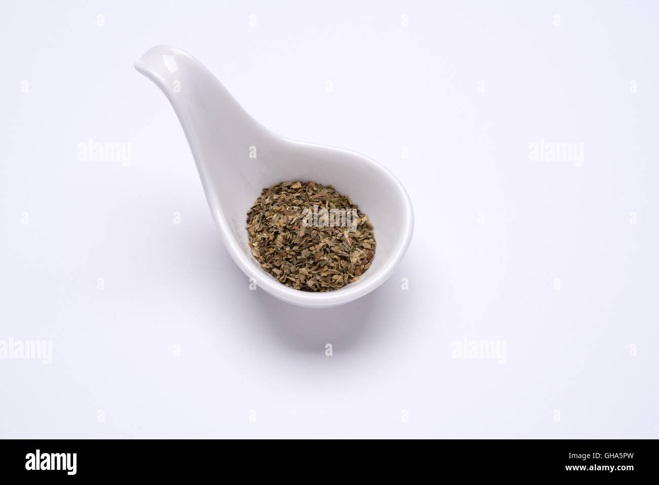 Monotone dry Basil 1 tablespoon in a white spoon on the white ...
