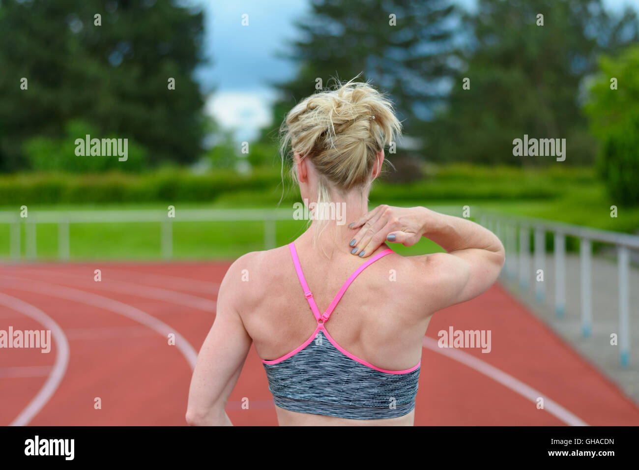 Rear view of athletic female sprinter massaging her own neck at race ...