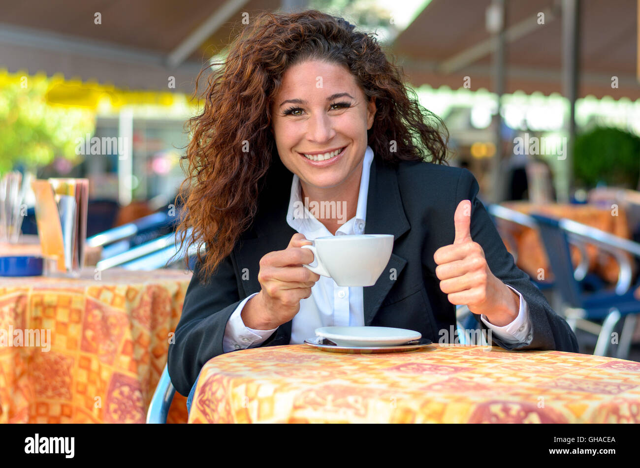 Happy young woman enjoying a cup of coffee at an open-air cafe looking ...