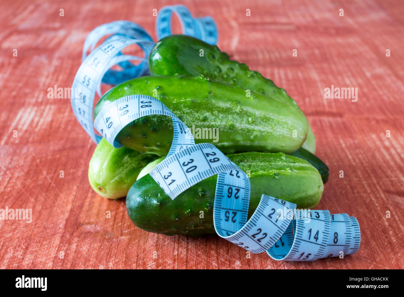 Cucumber fruits and tailor measuring tape on grey wooden background ...