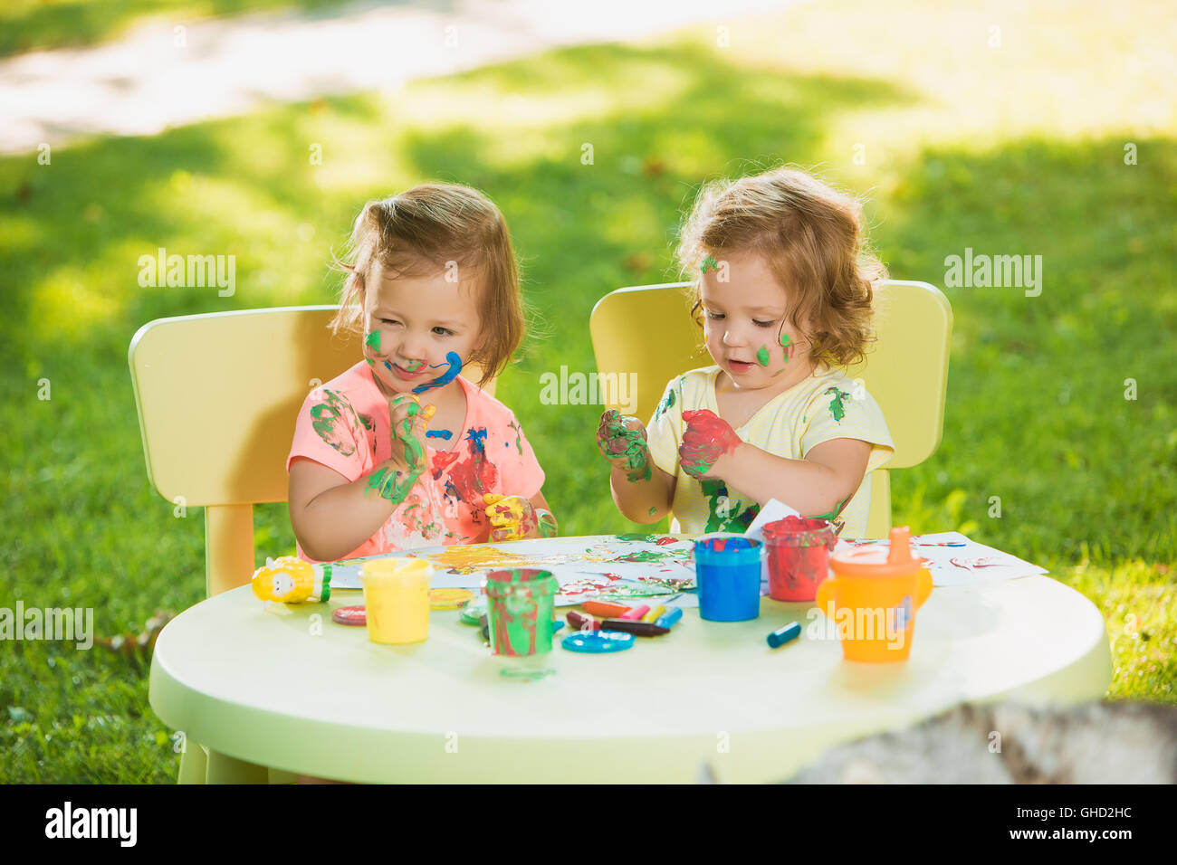 Two-year old girls painting with poster paintings together against ...