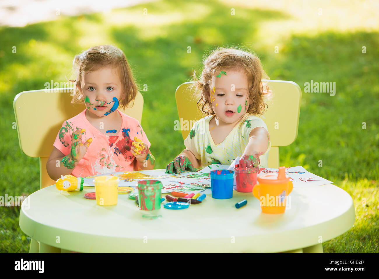 Two-year old girls painting with poster paintings together against ...