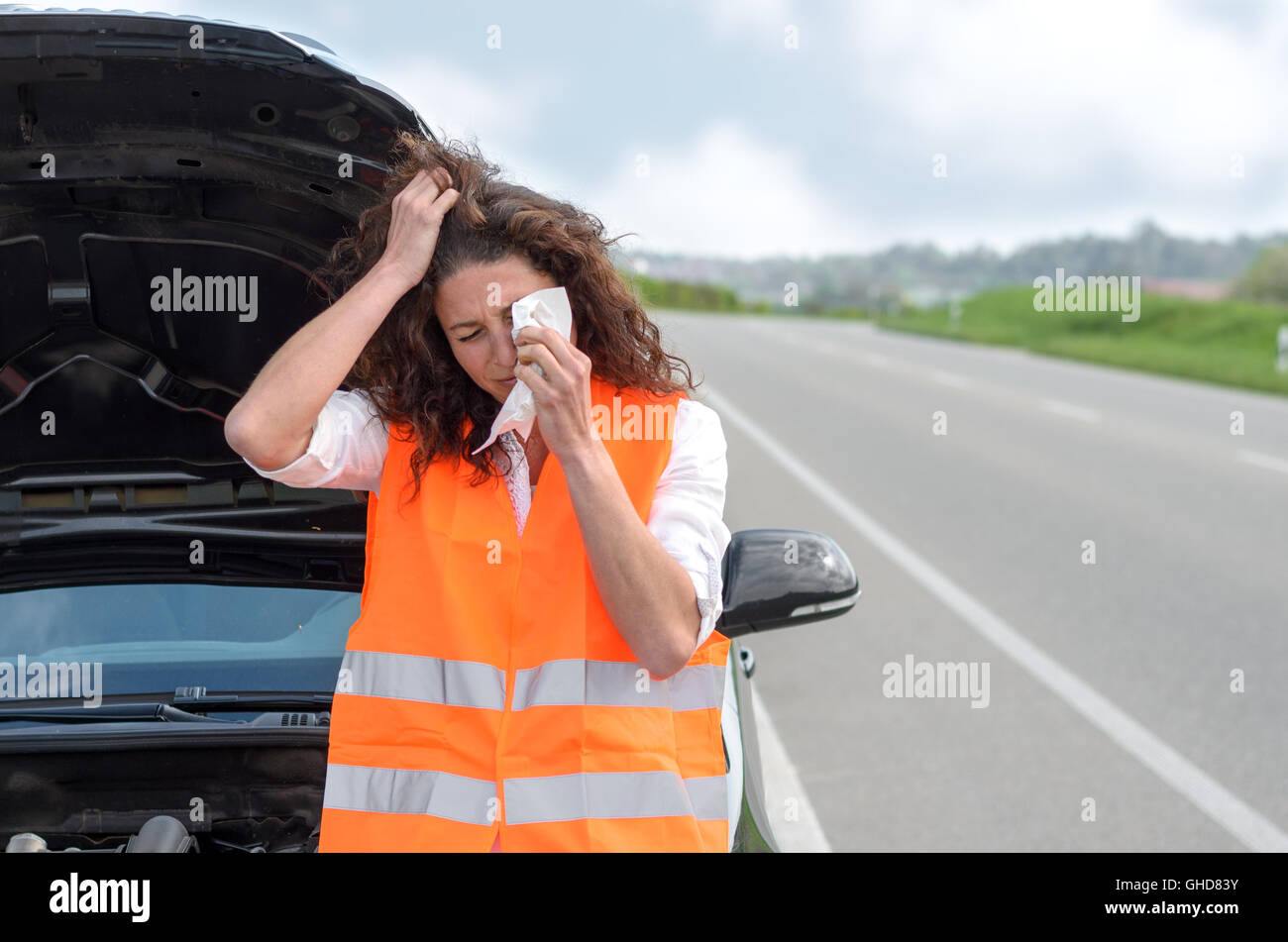 Upset young woman crying after a car breakdown standing wiping tears ...