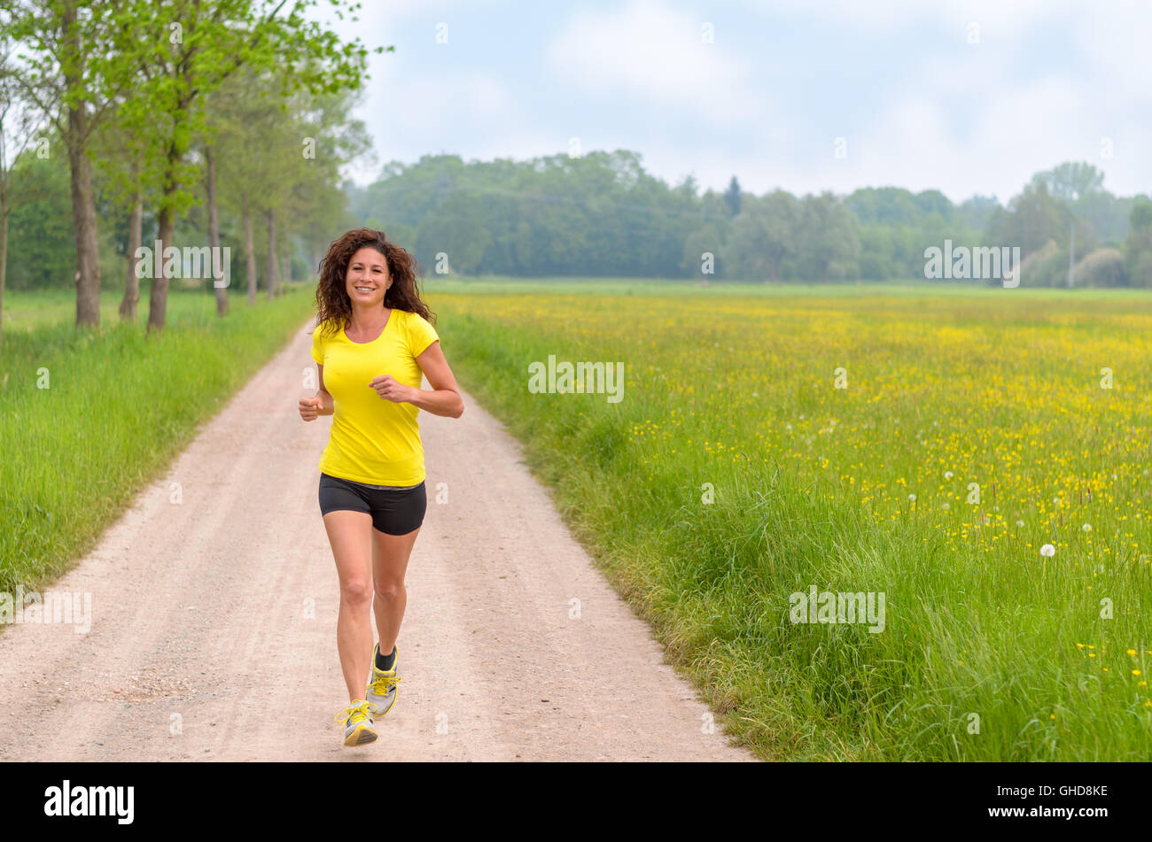 Smiling healthy young woman jogging in nature approaching the camera ...