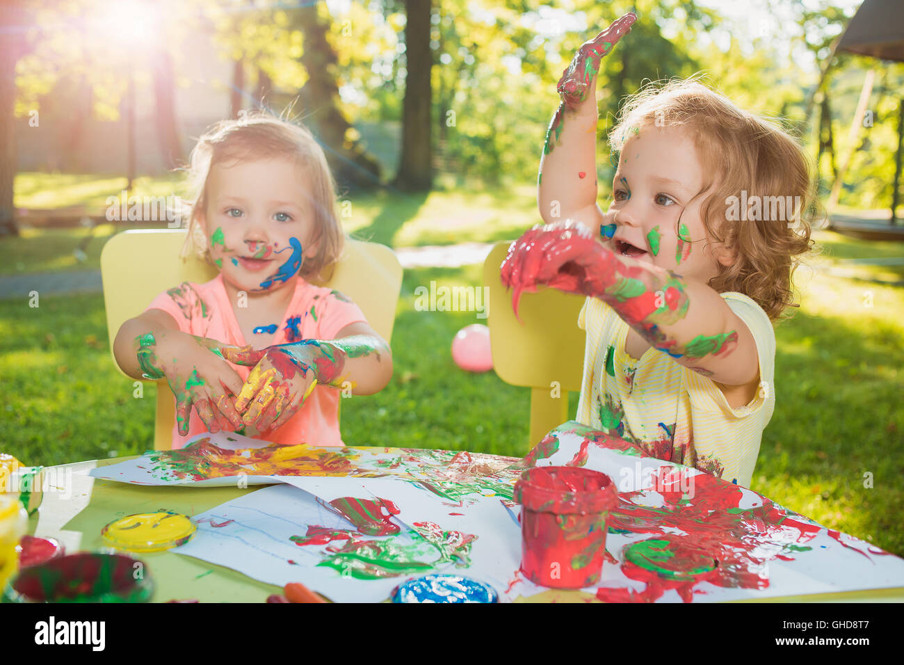 Two-year old girls painting with poster paintings together against ...