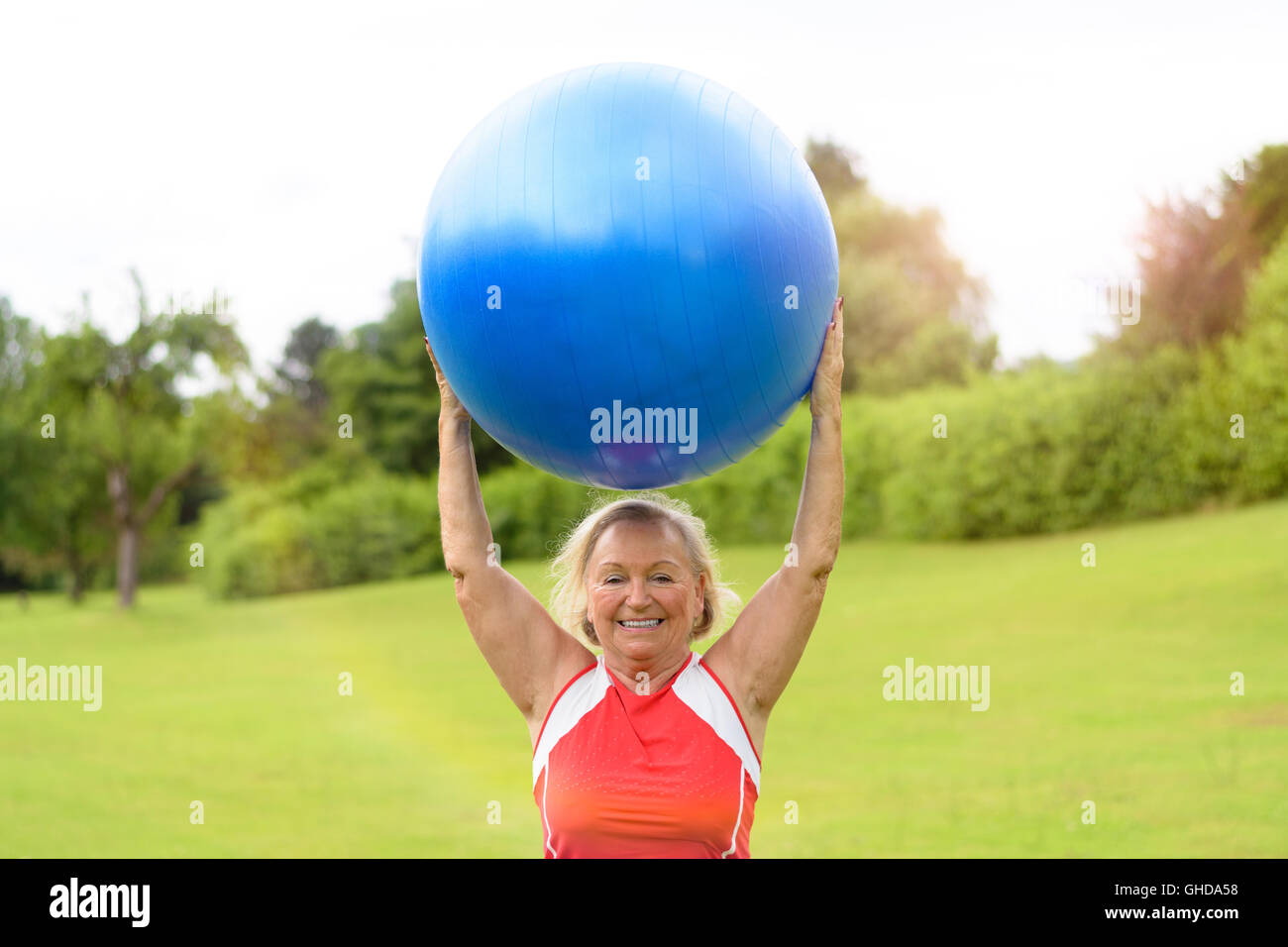Happy senior woman lifting inflated blue stability ball over head for ...