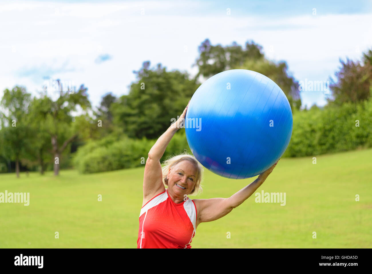 Happy senior woman lifting inflated blue stability ball over head for ...