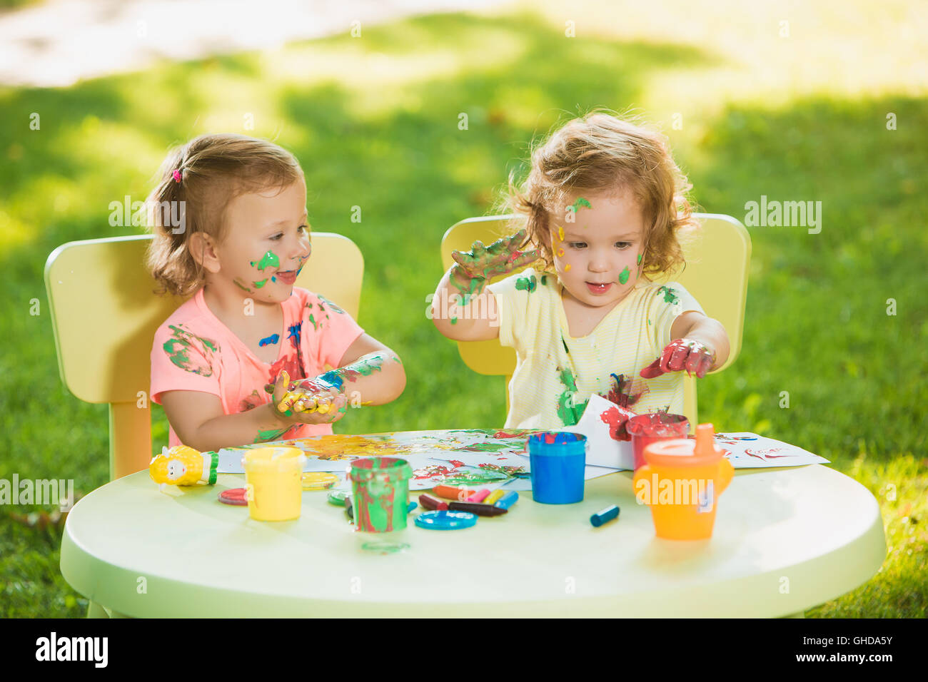 Two-year old girls painting with poster paintings together against ...