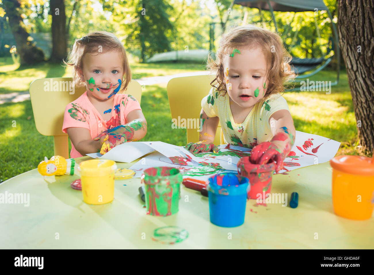 Two-year old girls painting with poster paintings together against ...