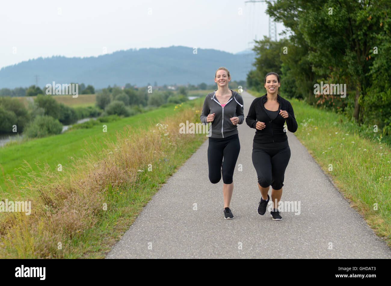 Two happy young women in sweatpants and jackets running on asphalt ...