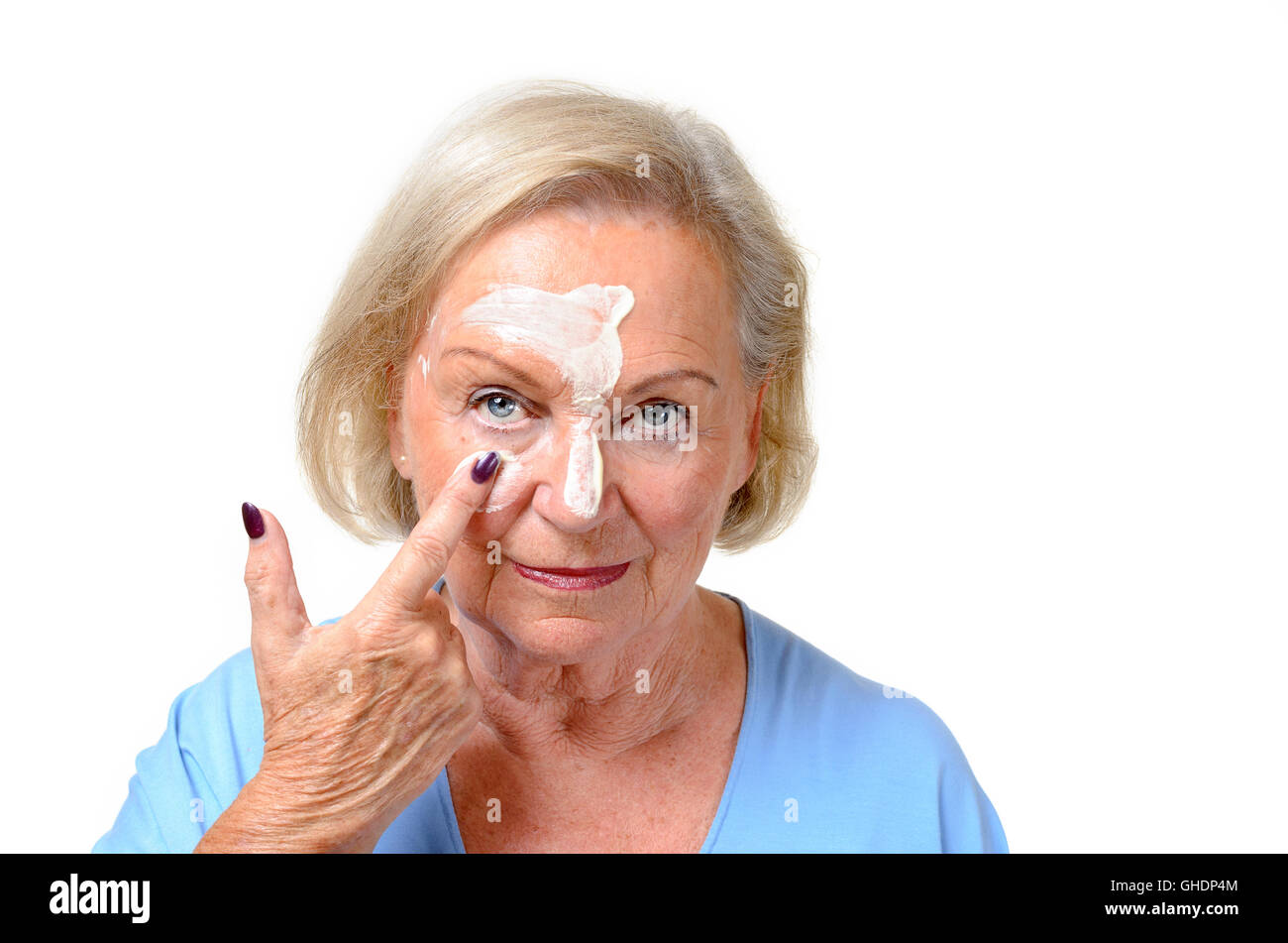 Attractive blond senior lady applying cosmetics to her face dabbing on ...