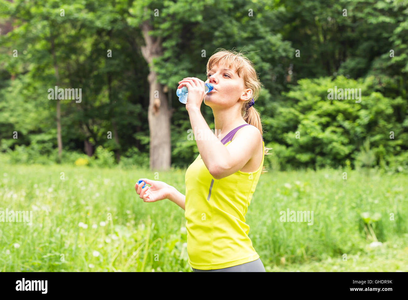 Fitness woman drinking water after work out exercising on summer ...