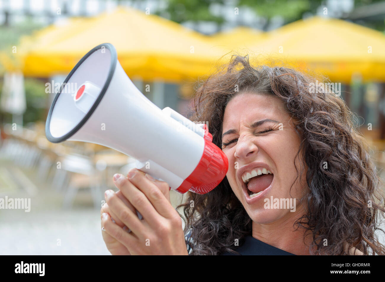 Attractive angry woman shouting into a megaphone outdoors n an urban ...