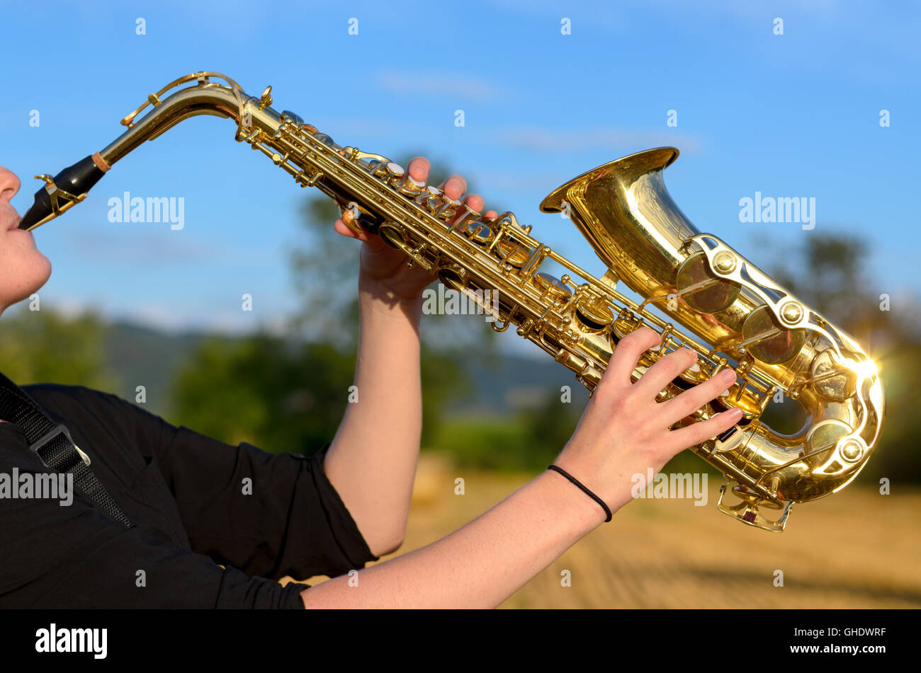 Side close up view of a young woman playing a tenor saxophone outdoors ...