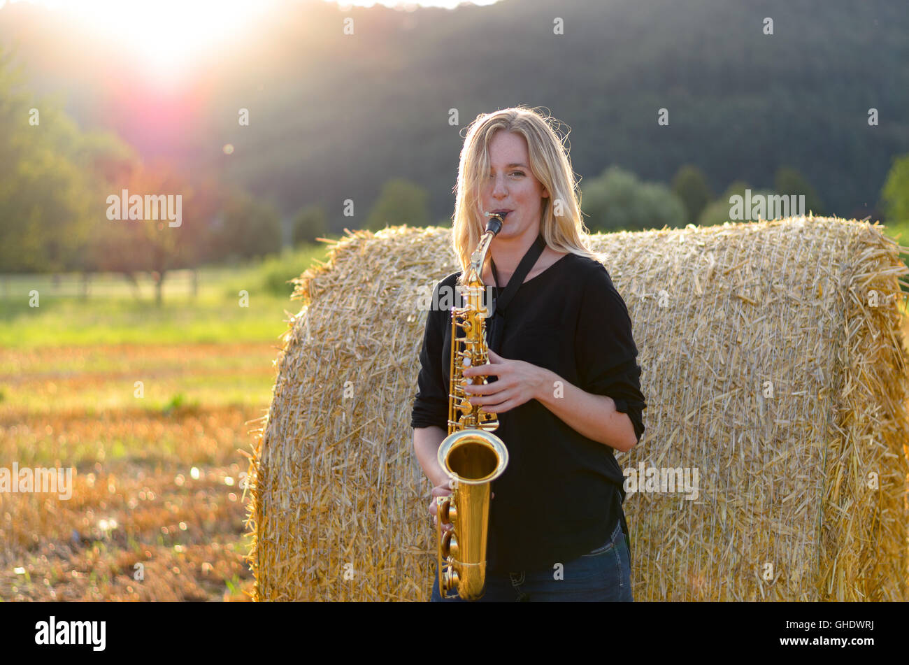 Attractive female musician playing a tenor saxophone as she leans ...