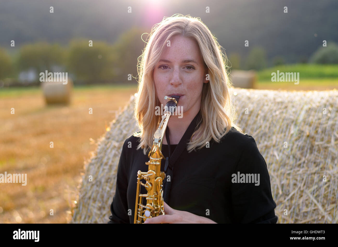 Attractive young woman playing a tenor saxophone as she stands outdoors ...