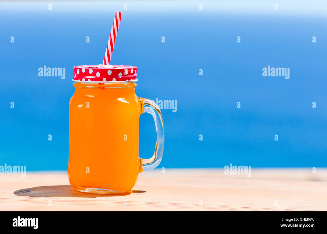 closeup of an orange beverage served in a glass mason jar with a red ...