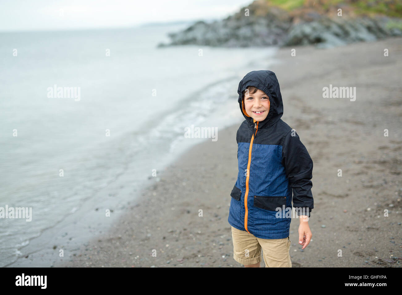 boy enjoying the rain and having fun outside on the beach a gray rainy ...