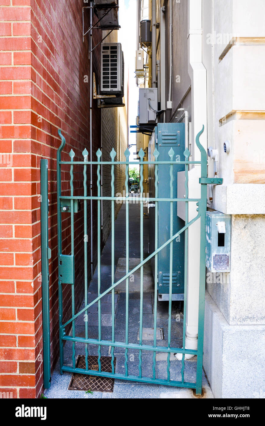 Green wrought iron gated entrance to alley between brick and stucco ...