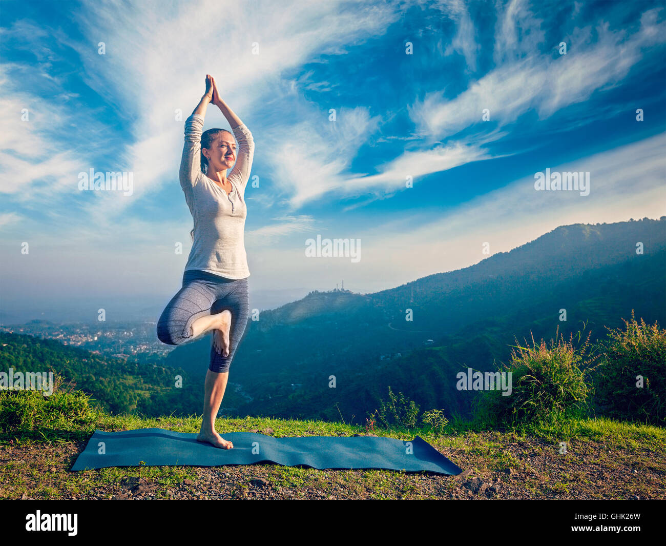 Woman doing yoga asana Vrikshasana tree pose in mountains outdoors ...