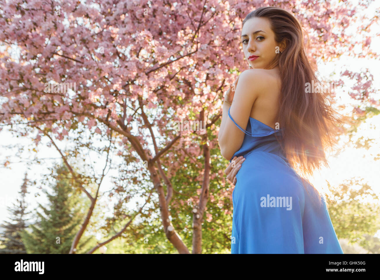 Back view of a beautiful young woman dressed in blue overalls standing ...