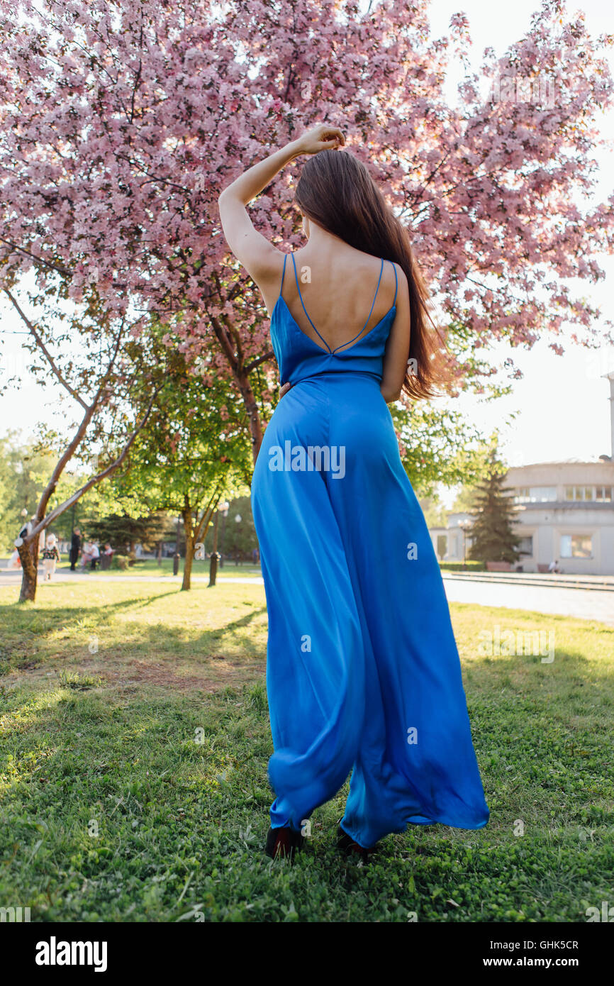 Back view of a beautiful young woman dressed in blue overalls standing ...