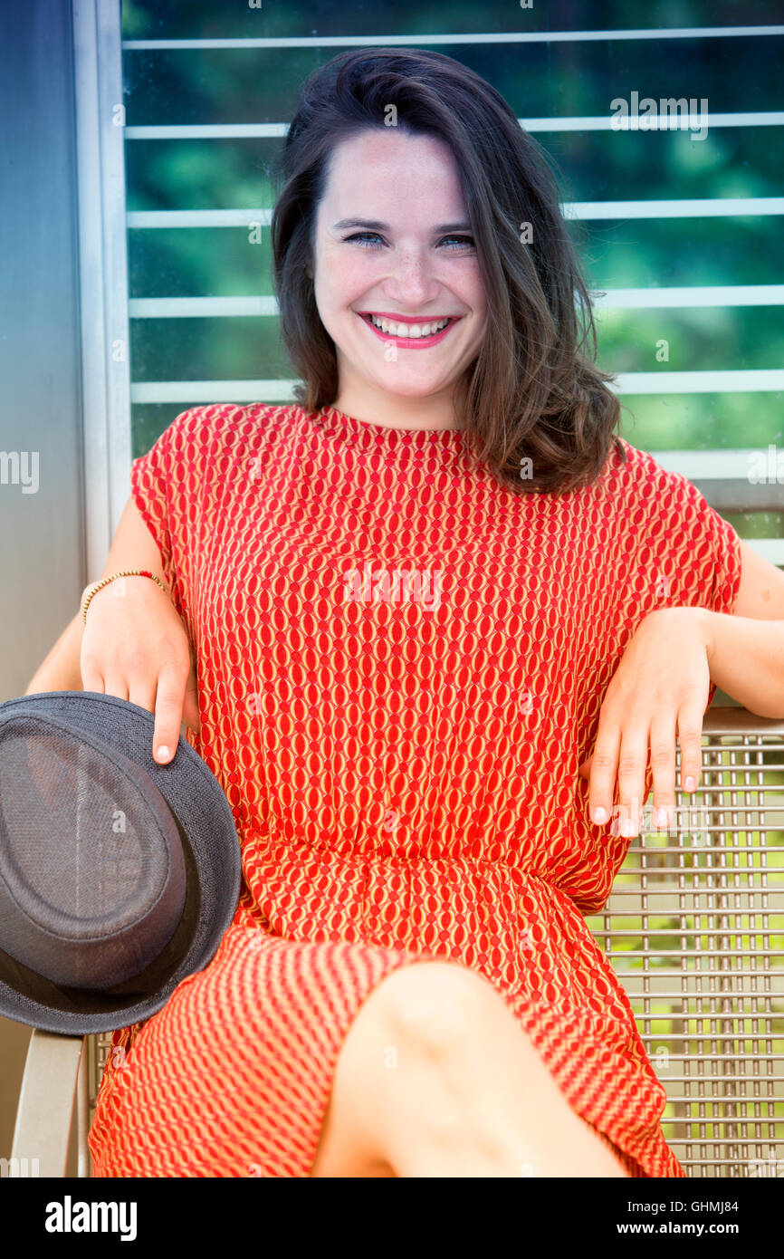 portrait of young woman in red dress sitting on bench and smiling at ...