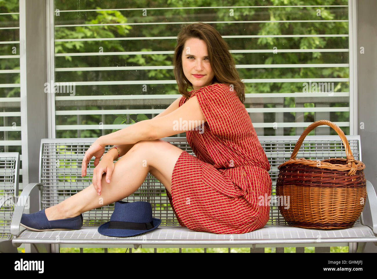 young woman in red dress sitting on bench with basket and smiles at ...
