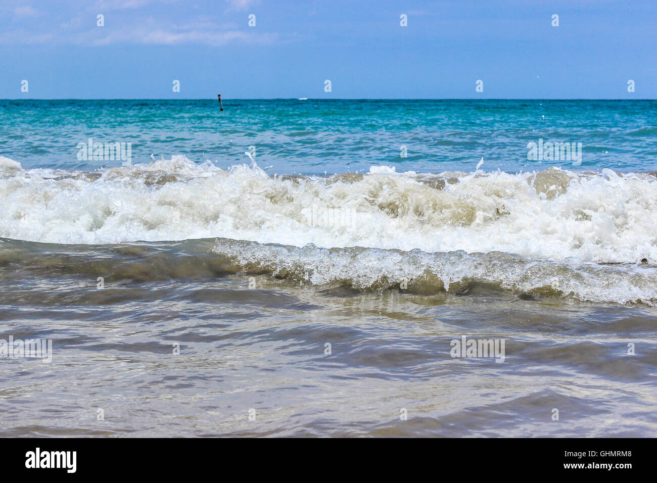Small wave breaking on beach in front of blue sky and turquoise sea ...