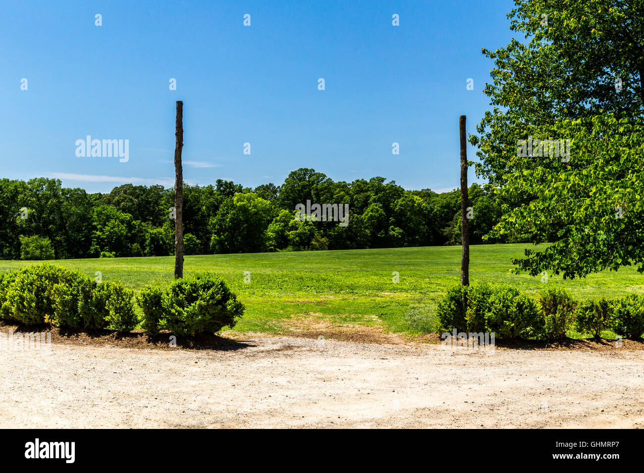 Two wood posts in the entrance of a grass field past a dirt and gravel ...