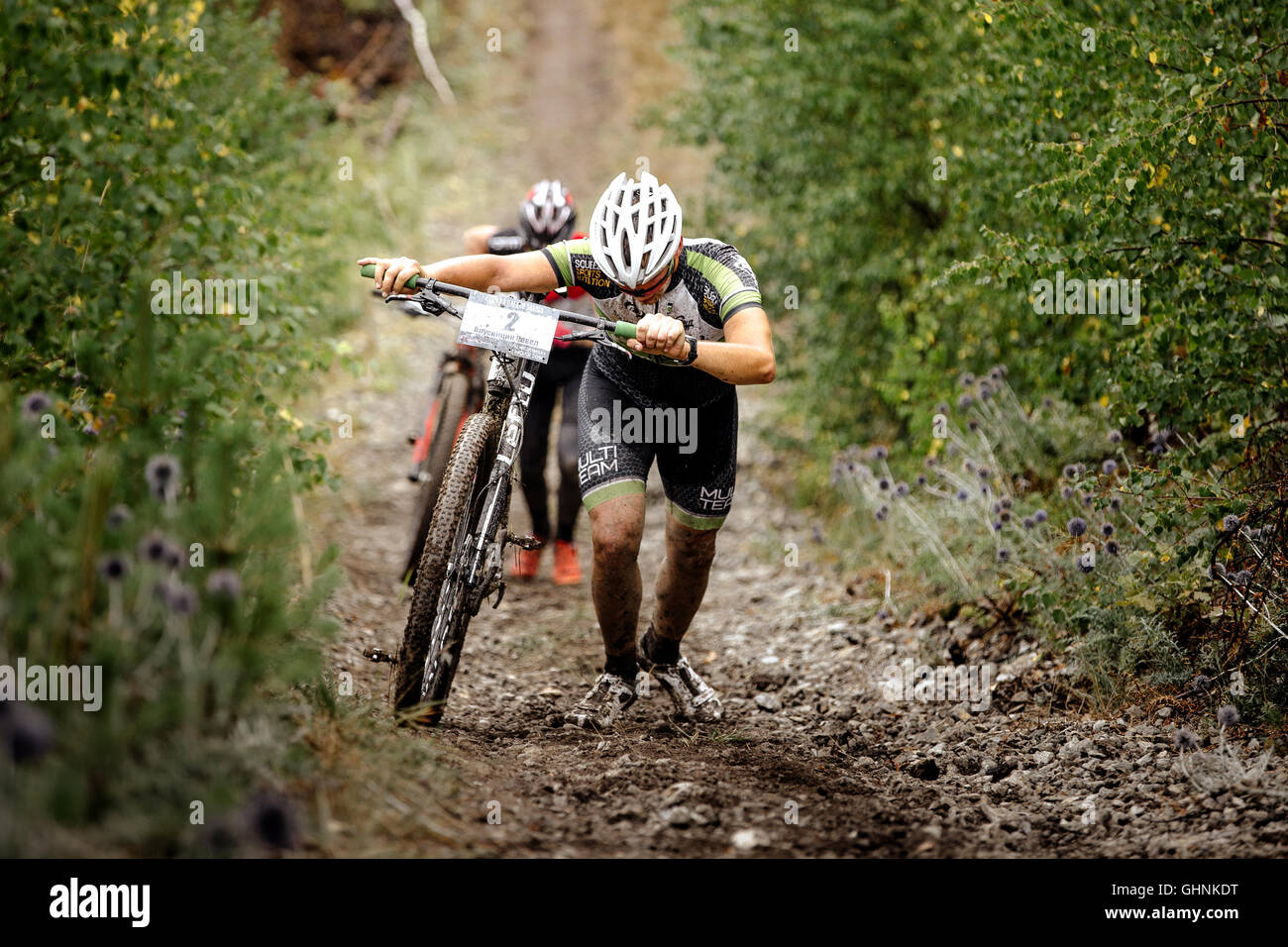 two men mountainbikers climb mountain on foot with their bicycle during ...