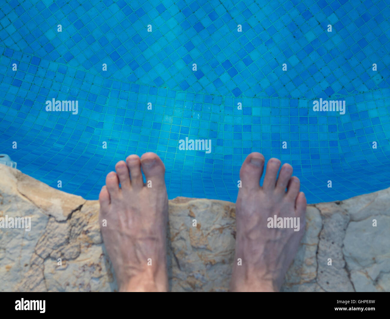 close-up of man's feet standing on edge of swimming pool with rippling ...