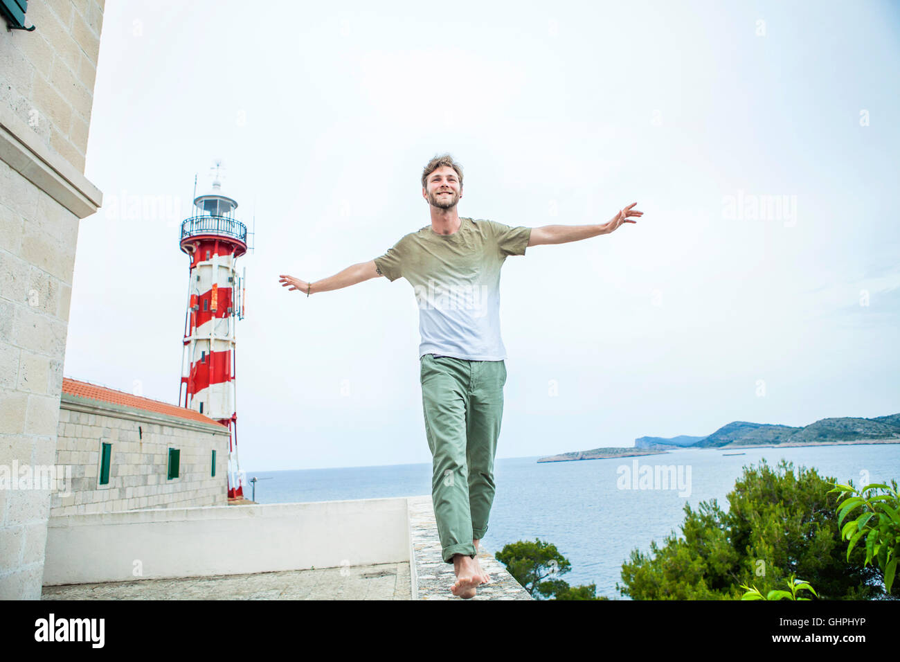 Young man balancing on wall with lighthouse in background Stock Photo ...
