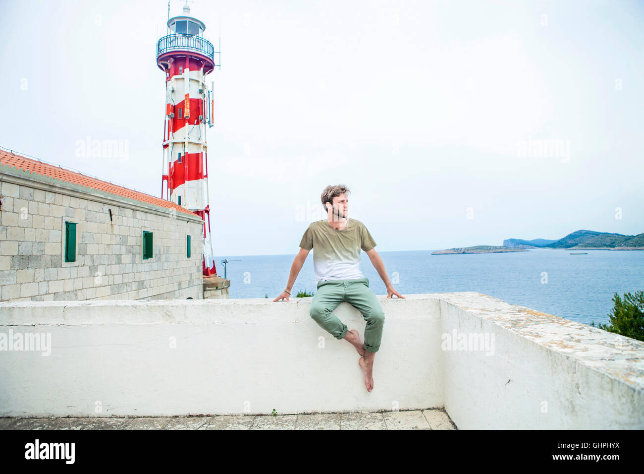 Young man sitting on wall with lighthouse in background Stock Photo - Alamy