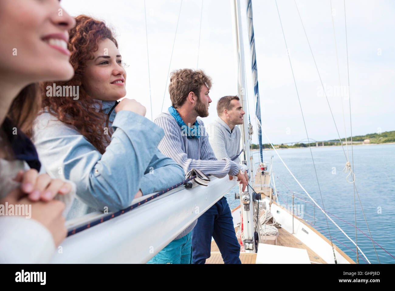 Group of friends leaning against boom of sailboat Stock Photo - Alamy