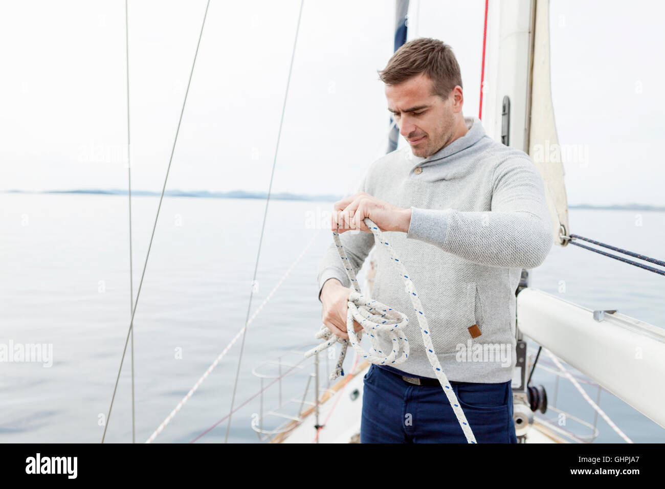 Man on yacht curling up rope Stock Photo - Alamy