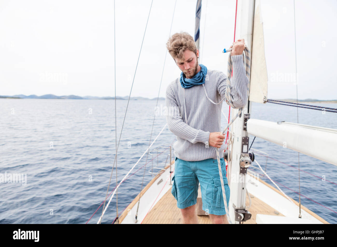 Young man on yacht curling up rope Stock Photo - Alamy