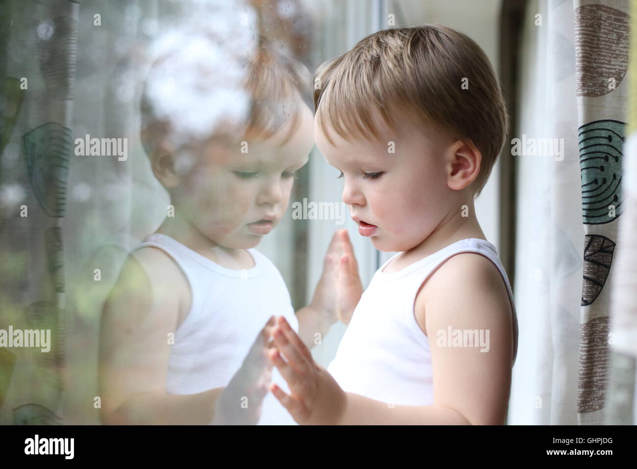 toddler boy stares out of window looking at his reflection Stock Photo ...
