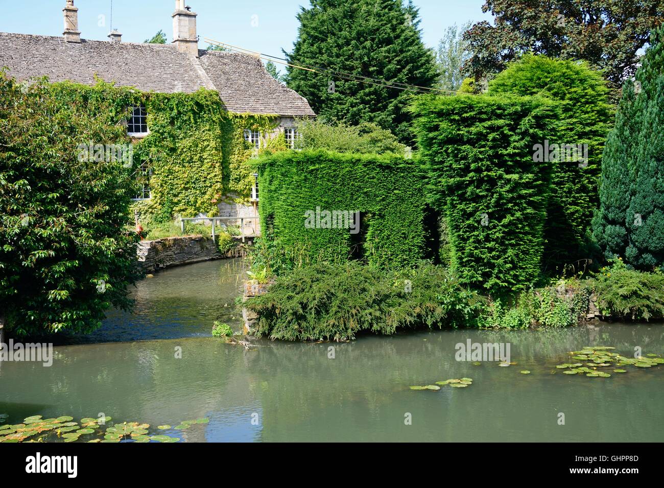 Cotswold stone cottage alongside the River Windrush with a weir in the ...