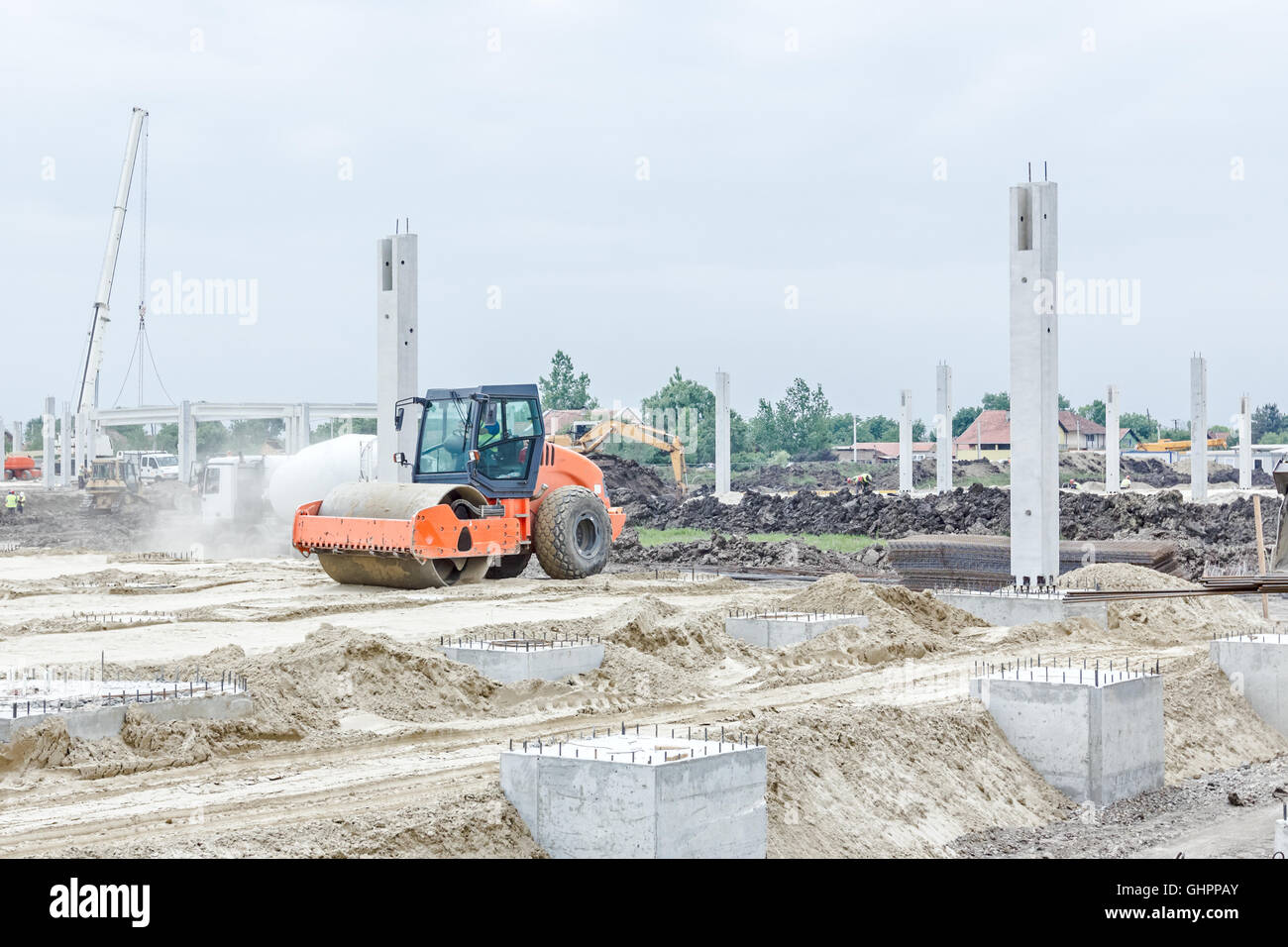 Steamroller is compacting sand among base pillars, passing over ...