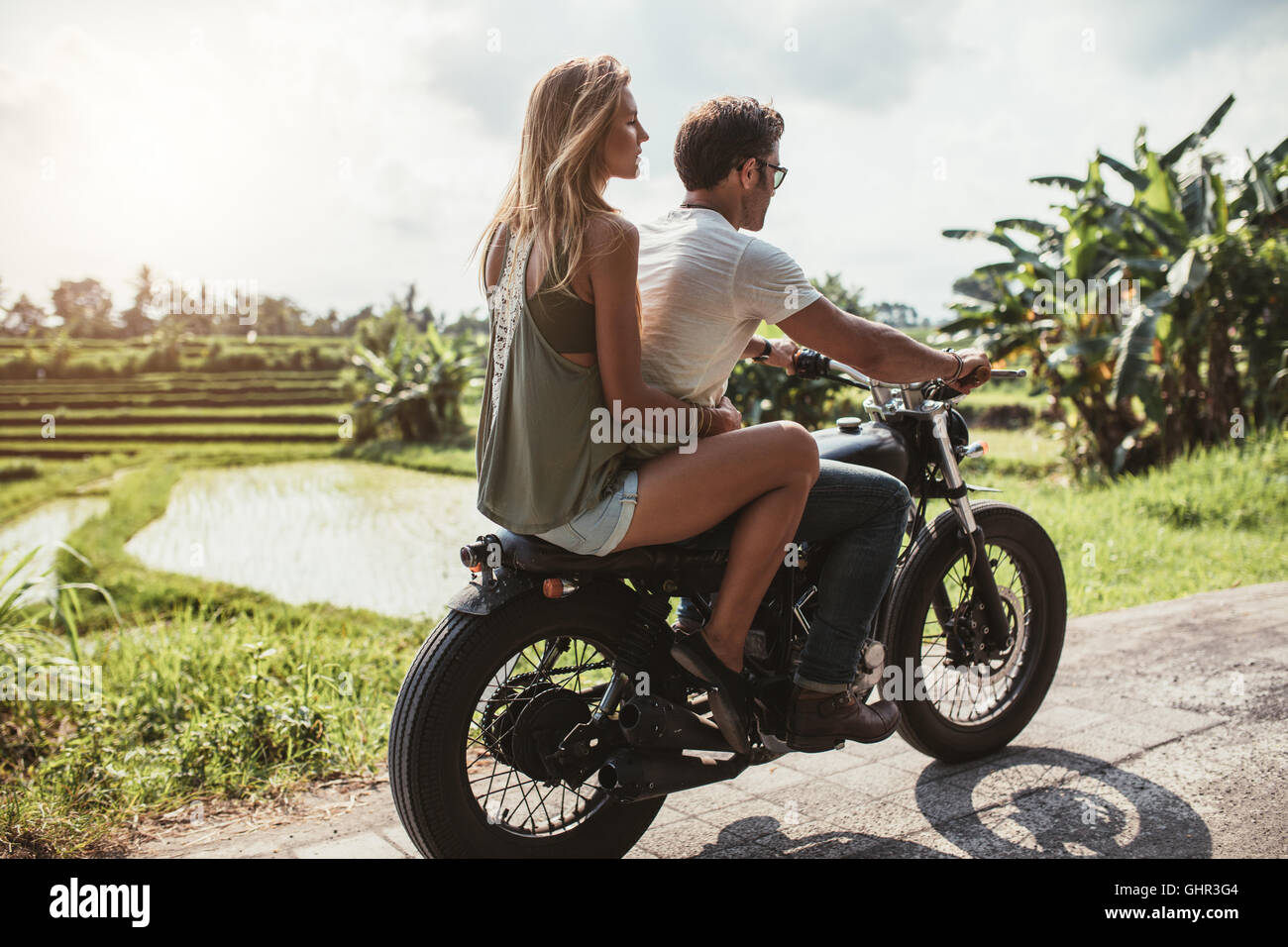 Man riding motorcycle with a woman on rural road. Young couple on ...