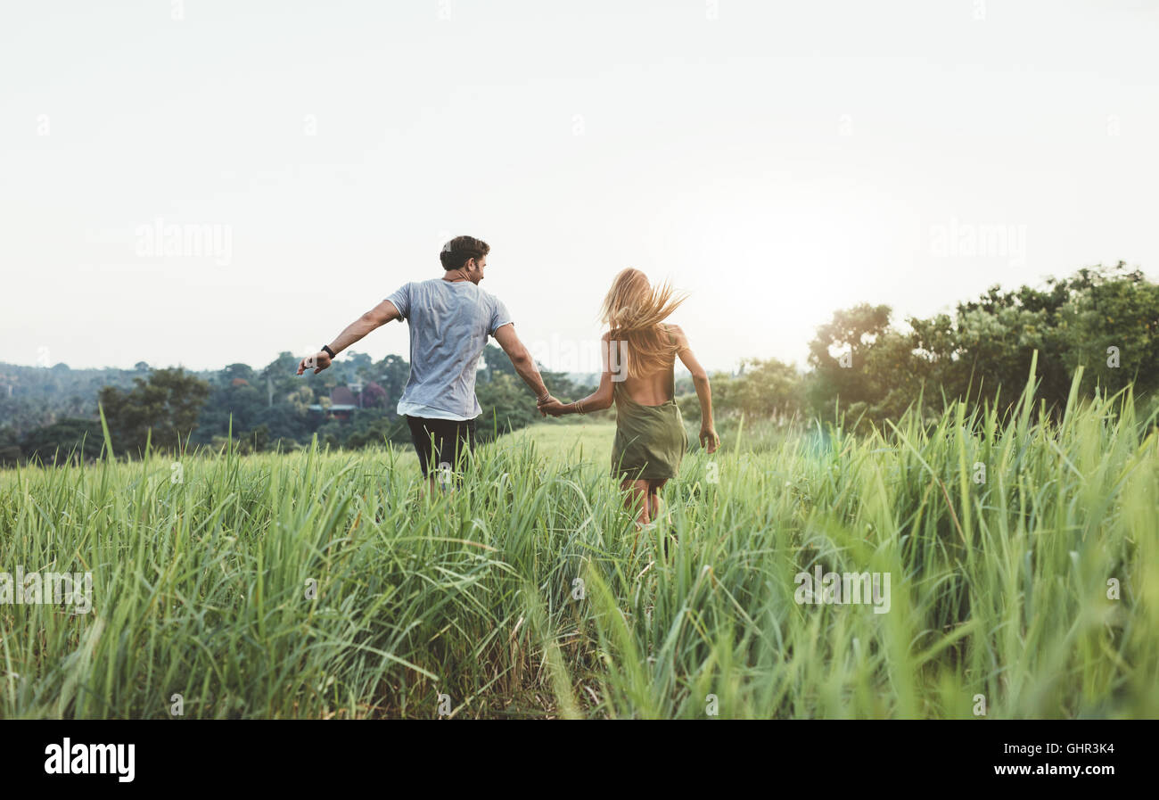Rear view shot of young man and woman holding hands running through ...