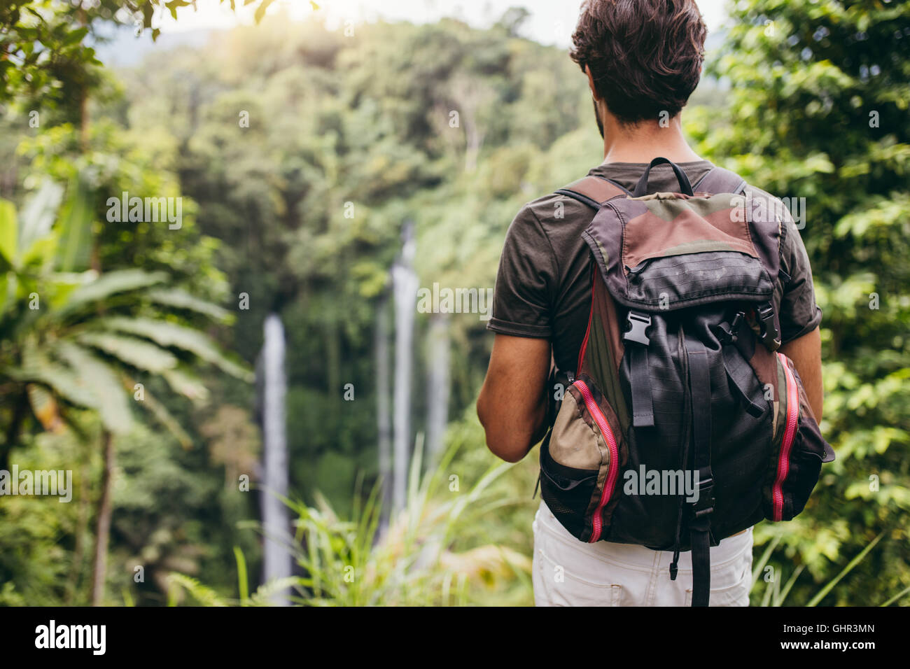 Rear view shot of male hiker with backpack standing on a cliff and ...