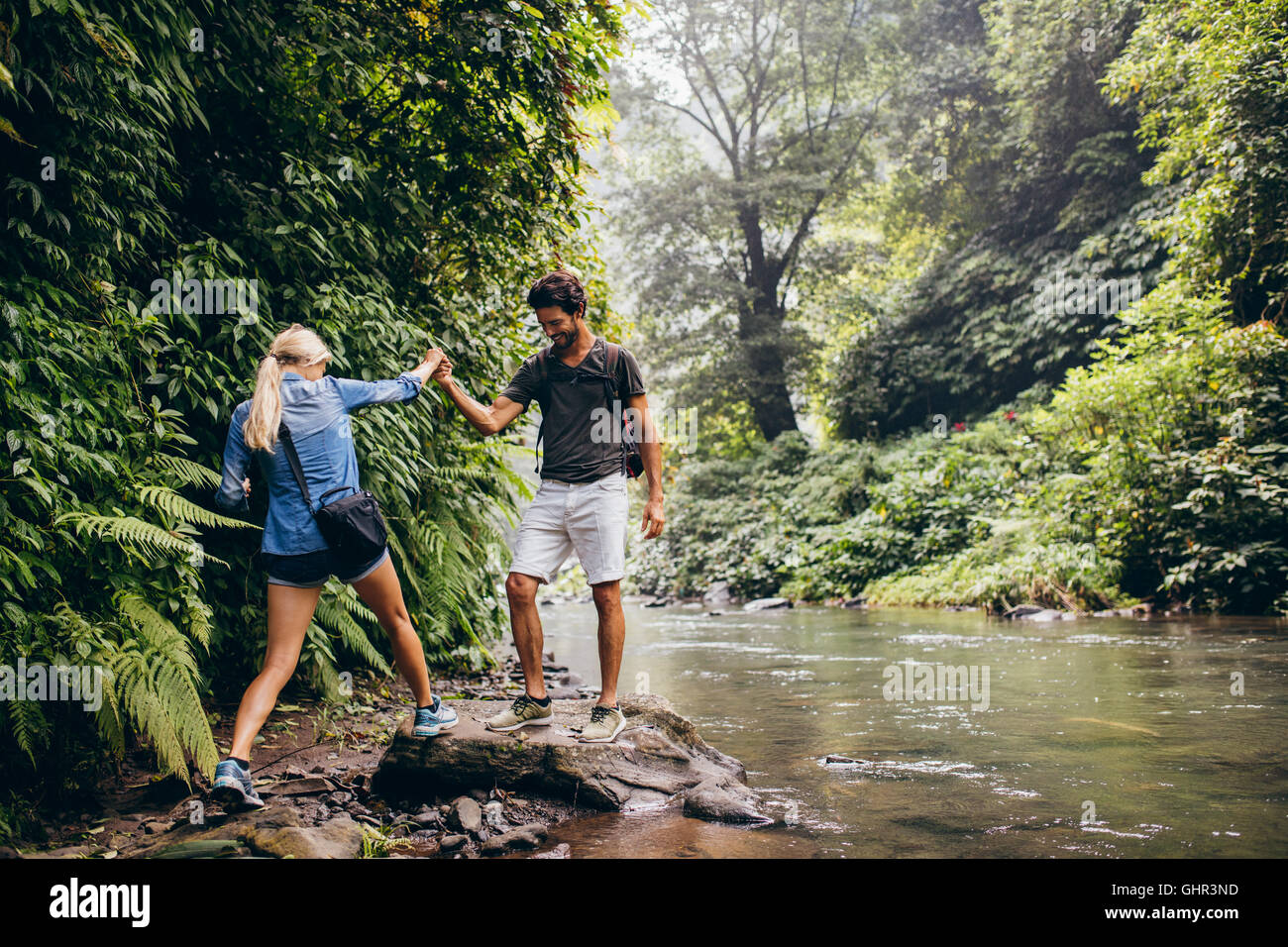 Couple of hikers in forest. Young man helping woman while walking by ...