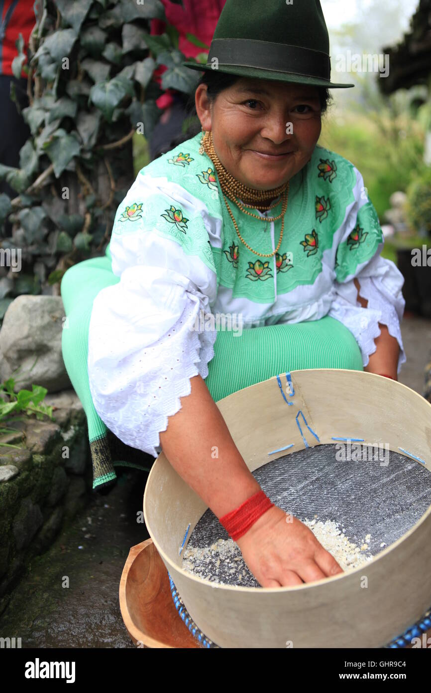 A traditionally dressed, older Ecuadorian woman, hand sieves corn into ...