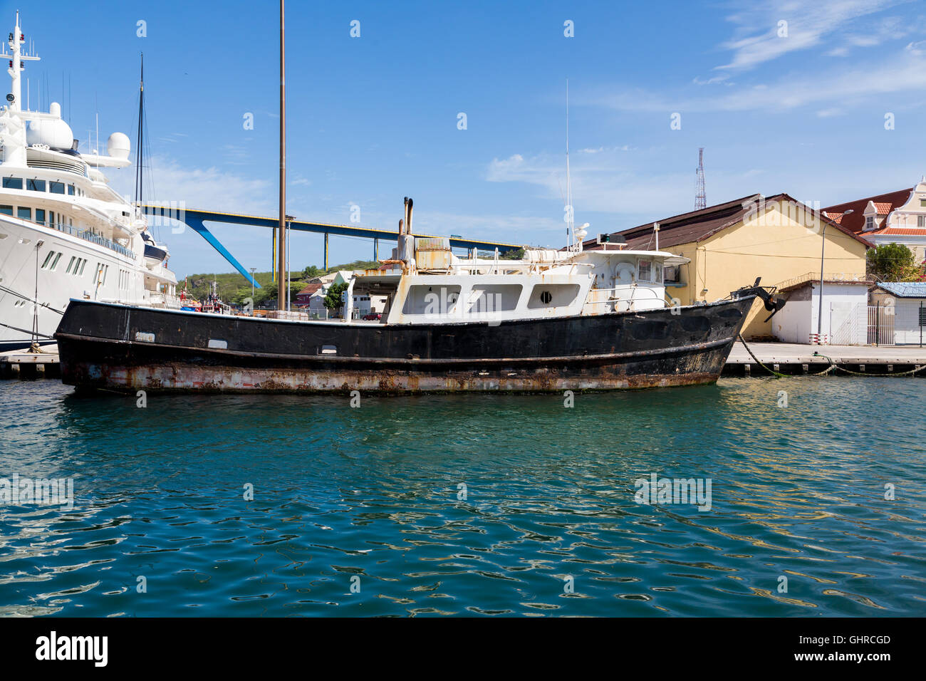 Rusty Black Boat by White Yacht in Curacao Stock Photo - Alamy