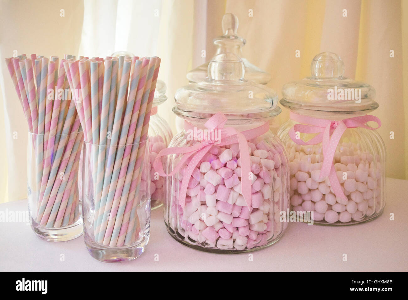 Horizontal view of jars of pink sweets and old fashioned paper straws ...