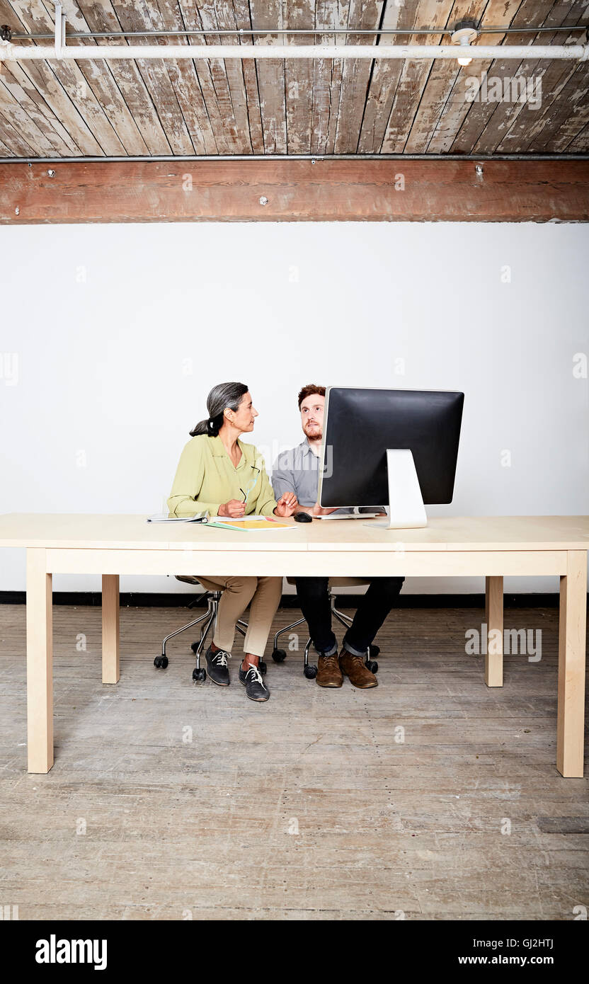 Colleagues at desk behind computer monitor Stock Photo - Alamy