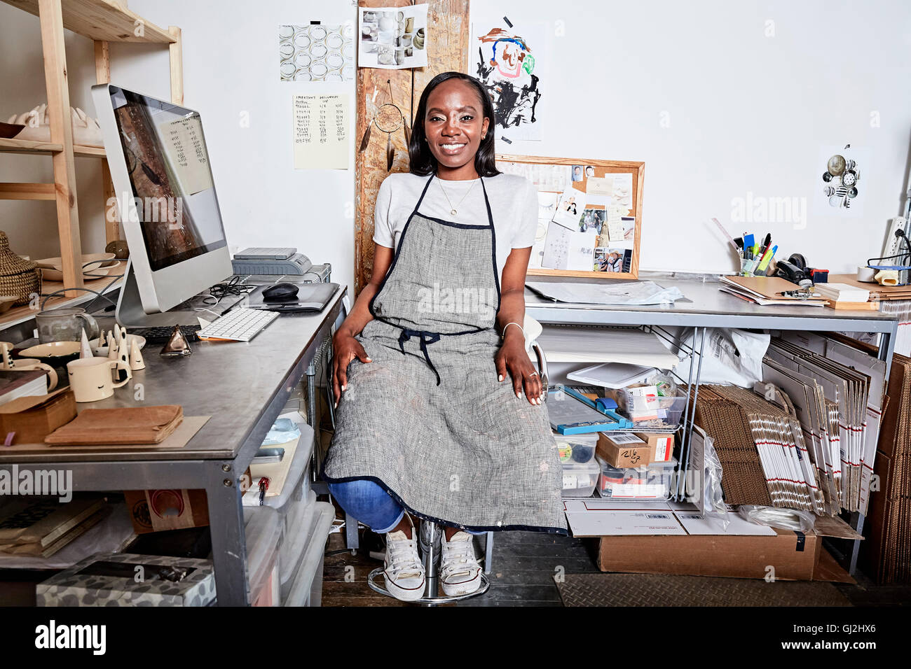Woman at desk wearing apron looking at camera smiling Stock Photo - Alamy