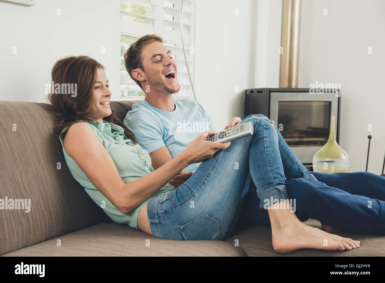 Couple on sofa using remote control laughing Stock Photo - Alamy